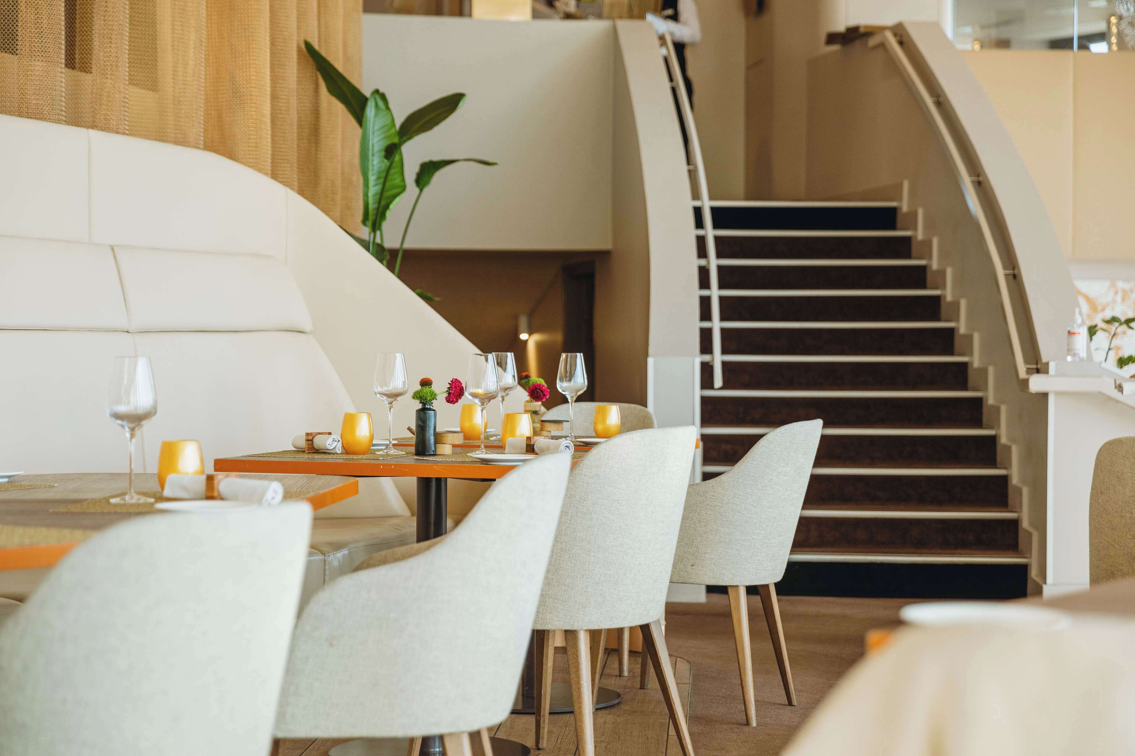 Uma área de refeições com uma mesa posta para dois, uma escada e uma planta ao fundo.