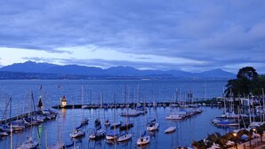 Uma marina com vários barcos atracados, um pequeno farol e montanhas ao fundo.