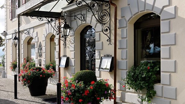 A building with a sign reading "RESTAURANT" above the entrance, potted plants with flowers, and a wrought iron gate.