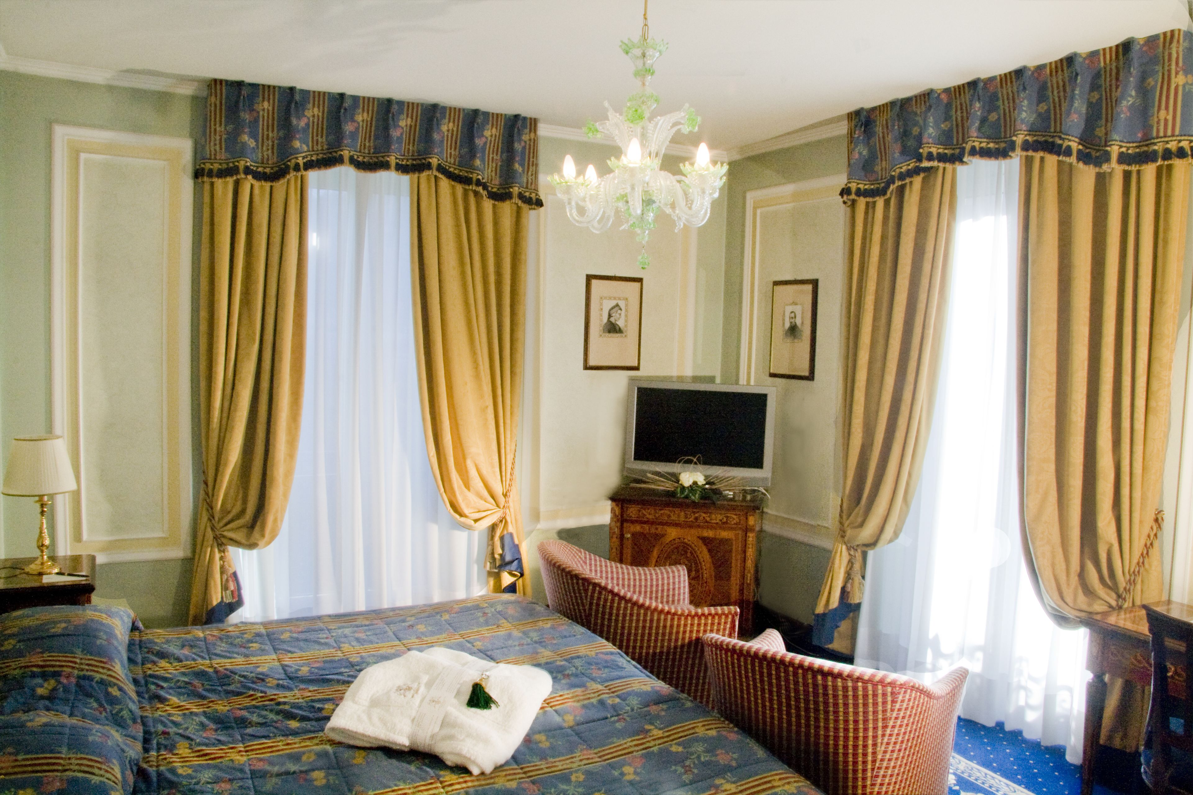 Quarto de hotel com uma cama grande, televisão, mesinha e uma cadeira.