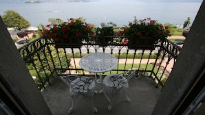 Uma varanda com duas cadeiras de metal e uma mesa pequena, com vista para um lago e montanhas ao fundo.