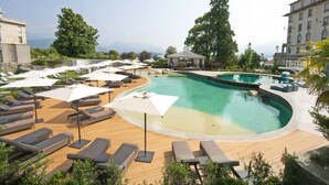 Uma área de piscina com espreguiçadeiras e guarda-sóis, cercada por vegetação e com vista para uma paisagem montanhosa.