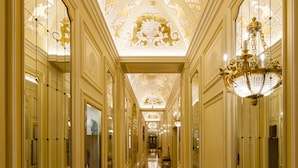 Um corredor longo e ricamente decorado, com paredes espelhadas e um candelabro.