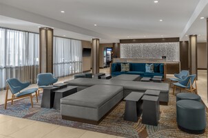 Um hall de hotel moderno com um amplo sofá modular, poltronas azuis e um tapete estampado.
