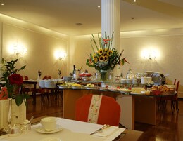 Espaço de refeições de hotel com serviço de buffet, incluindo diversos alimentos e uma máquina de café.