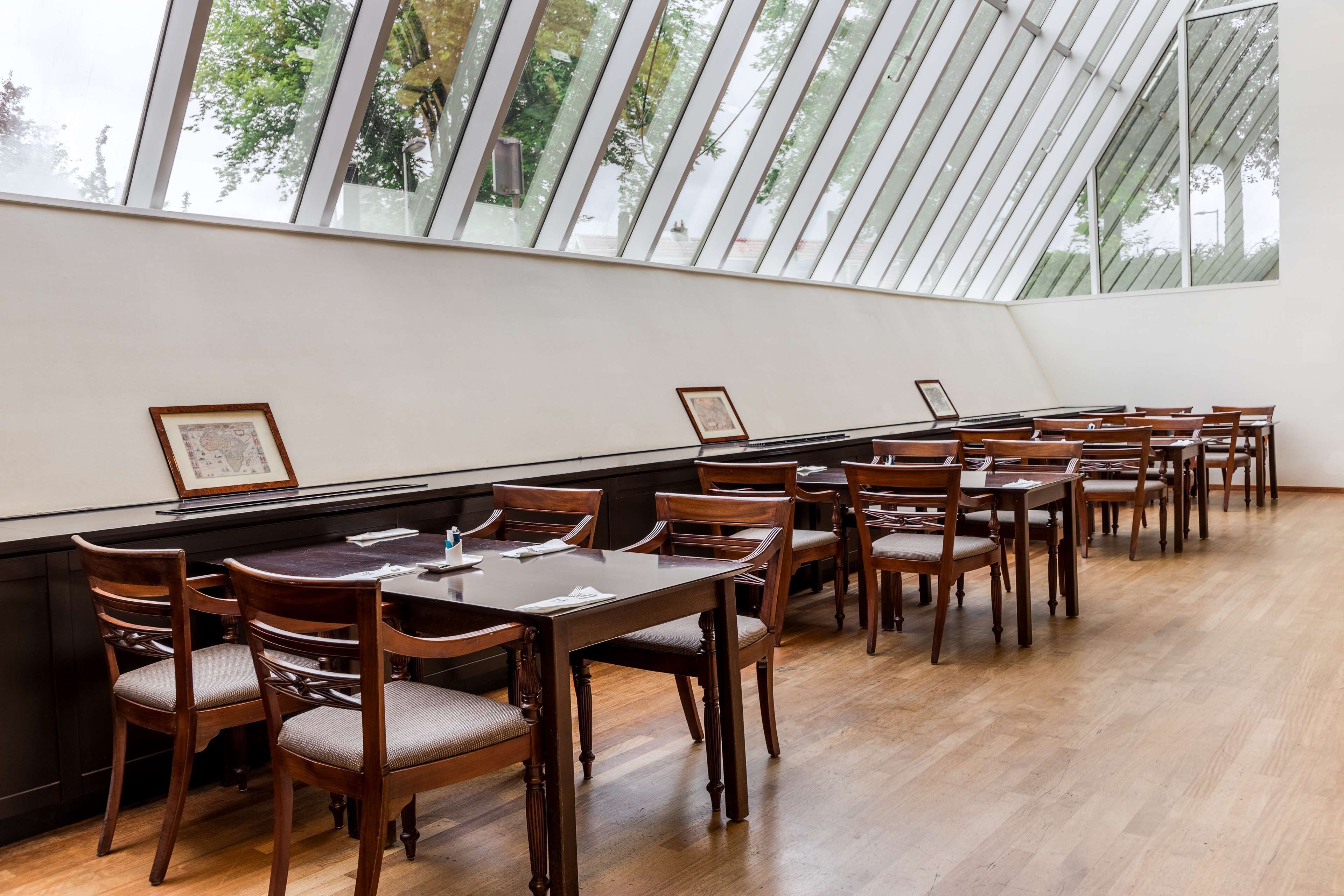 Uma sala de conferências com uma mesa comprida e várias cadeiras, janelas amplas com vista para árvores e quadros nas paredes.