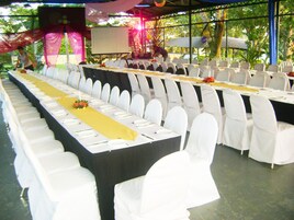 Uma longa mesa de banquete posta com cadeiras brancas, um caminho de mesa amarelo e uma tela de projeção.