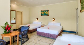 Quarto de hotel com duas camas, uma mesa pequena com uma cadeira, uma planta decorativa e um quadro na parede.