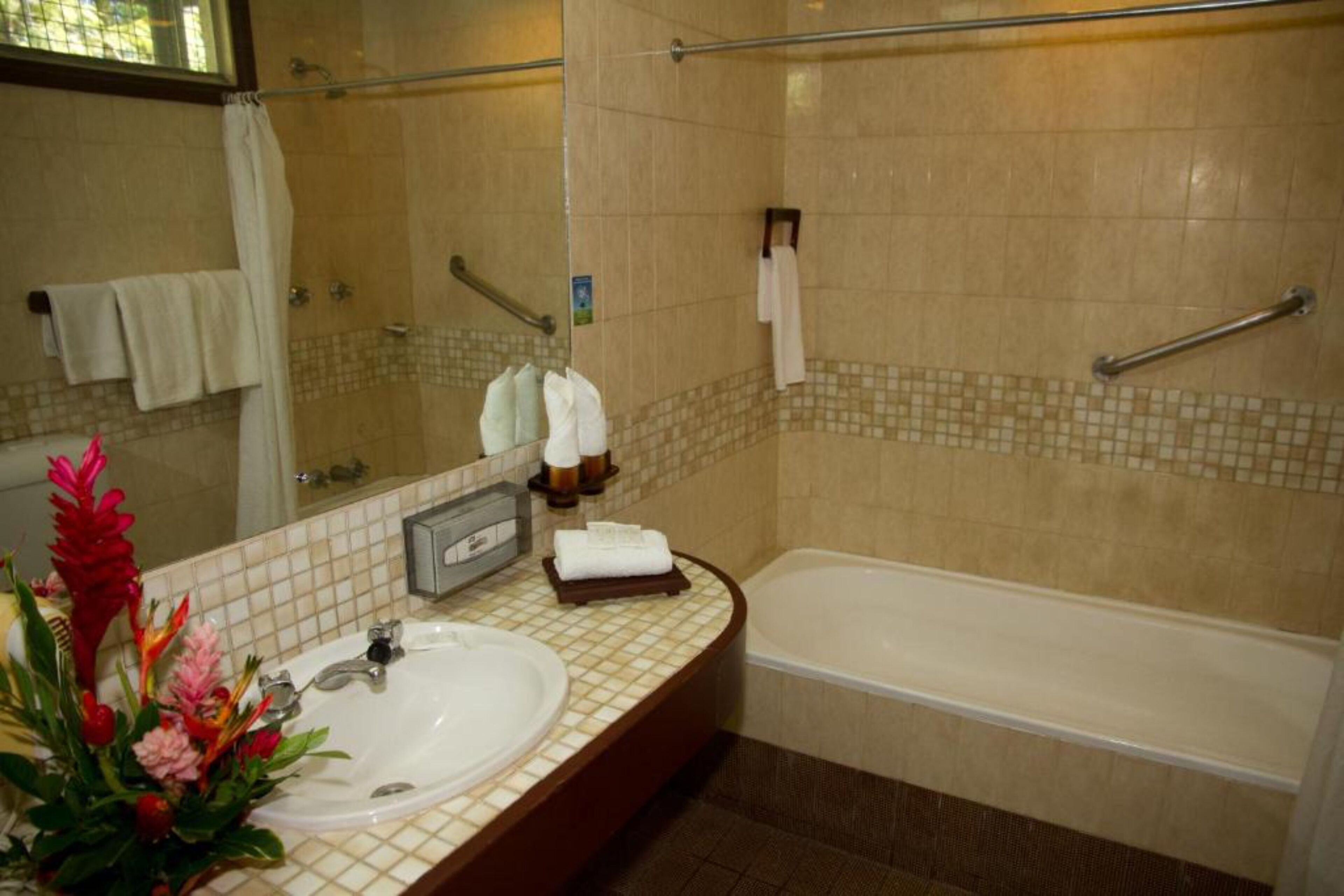 Casa de banho com lavatório, espelho e banheira. Há toalhas e produtos de higiene no balcão.