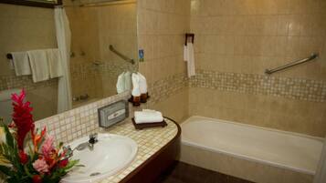 Casa de banho com lavatório, espelho e banheira. Há toalhas e produtos de higiene no balcão.
