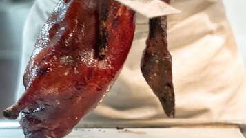 Uma pessoa com avental branco e luvas pretas segurando um pedaço grande de carne vermelha e uma faca.