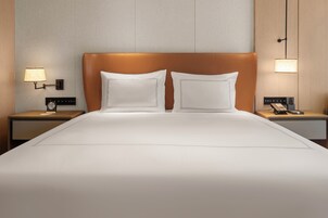 Quarto de hotel com uma cama grande, duas mesas de cabeceira, uma luminária na parede e um telefone.