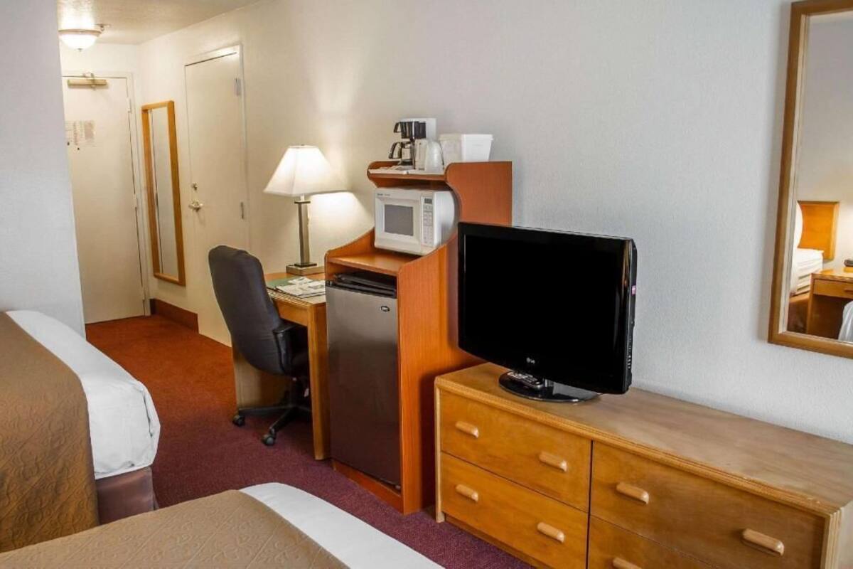 Quarto de hotel com cama, escrivaninha, frigorífico, micro-ondas, televisão e espelho.