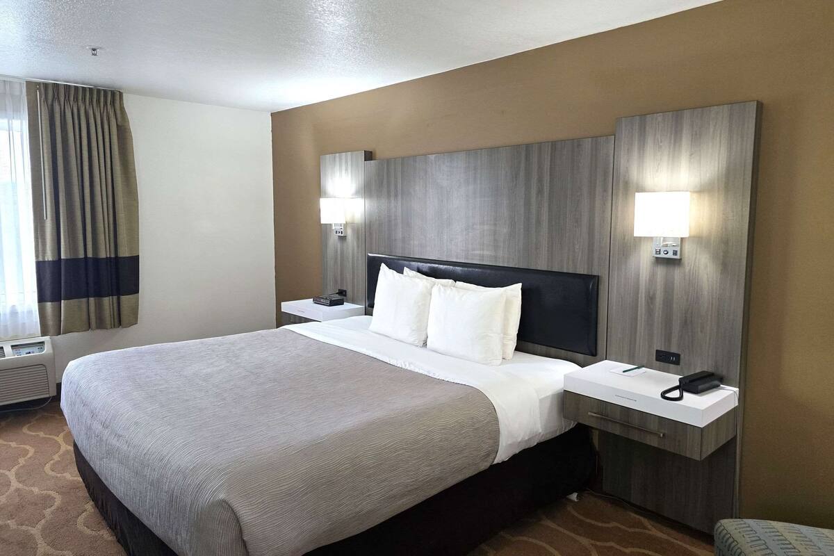 Quarto de hotel com uma cama grande, duas mesas de cabeceira, uma cabeceira e duas luminárias fixadas na parede.