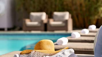 Uma área à beira da piscina com espreguiçadeiras, um chapéu de sol e toalhas.