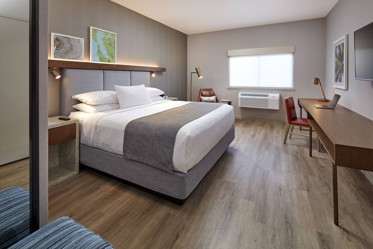 Quarto de hotel moderno com uma cama grande, uma escrivaninha, uma cadeira e uma janela com persianas.