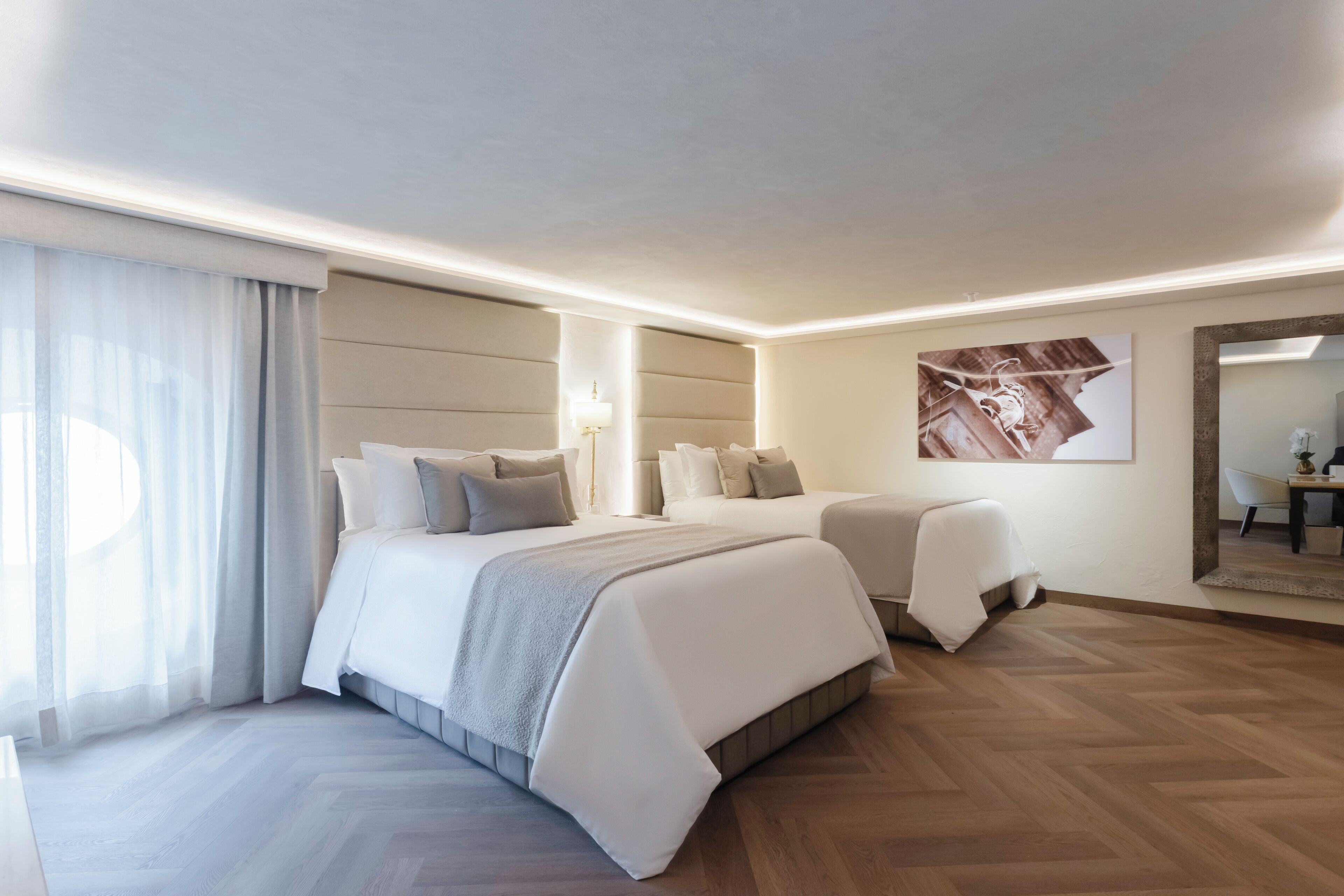 Quarto de hotel moderno com uma cama grande, uma cama menor, um espelho e um quadro na parede.