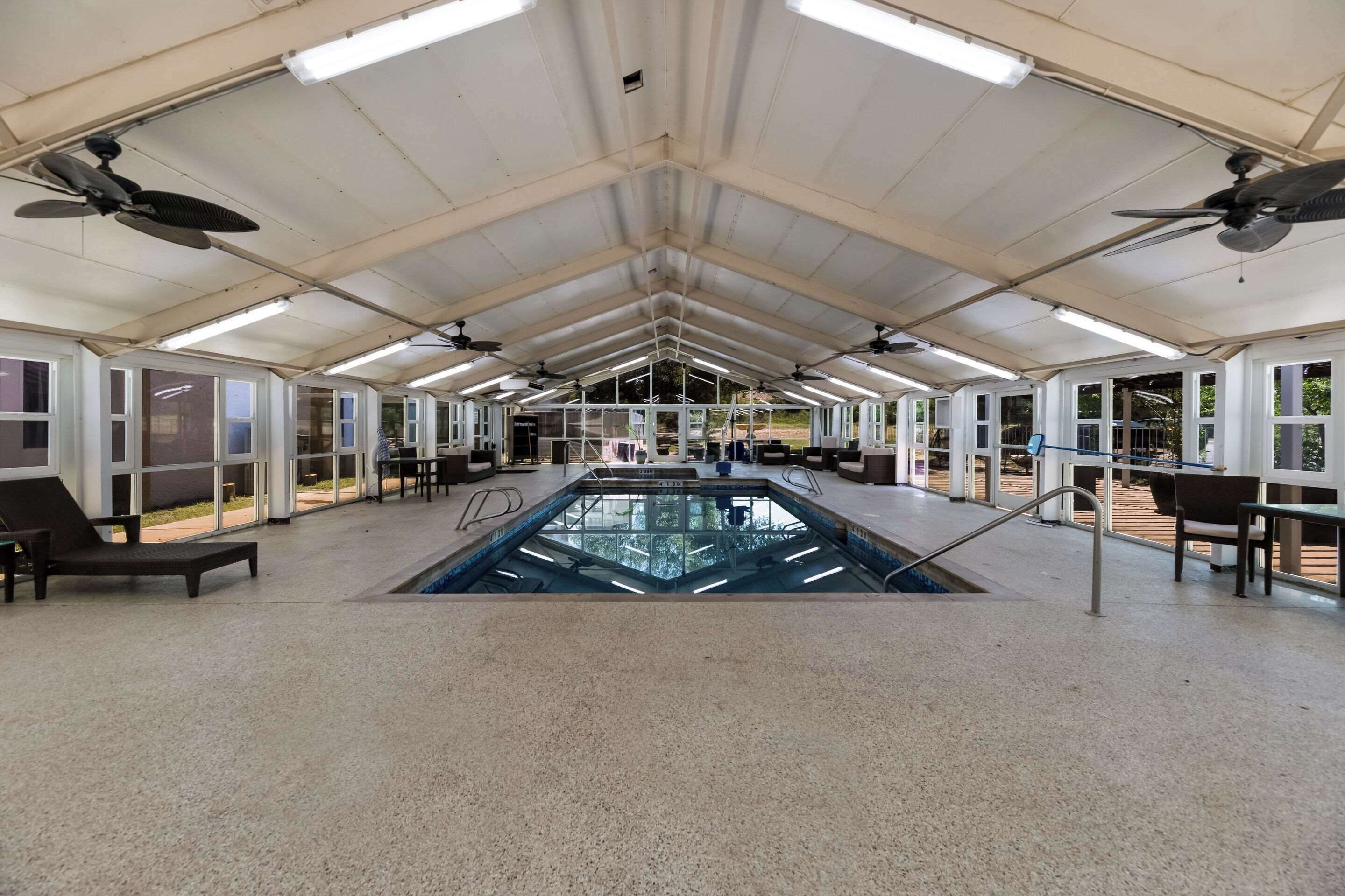 Uma área de piscina coberta com ventiladores de teto, espreguiçadeiras e piscina envidraçada.