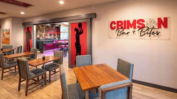 Interior de restaurante com mesas de madeira e cadeiras azuis, área de bar e placa com a inscrição 'CRIMSON Bar + Bites'.
