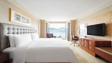 Quarto de hotel com uma cama grande, televisão, escrivaninha e vista para a paisagem urbana.