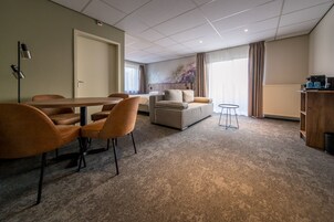 Quarto de hotel moderno com área de refeições, sofá e uma pequena mesa.