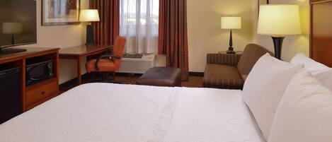 Quarto de hotel com uma cama grande, uma escrivaninha com cadeira, televisão e duas luminárias.