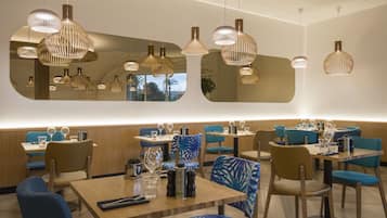 Um restaurante com várias mesas e cadeiras, luminárias pendentes e um espelho grande na parede.