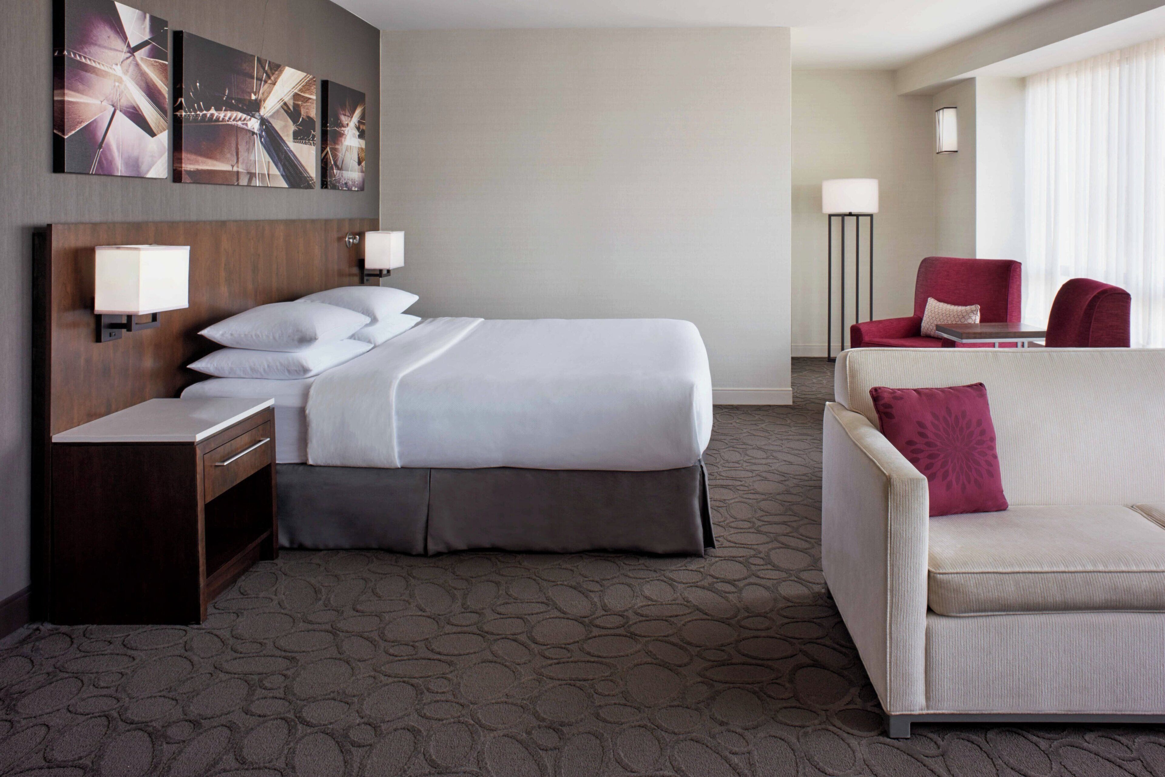 Quarto de hotel com uma cama grande, mesa de cabeceira com luminárias, um sofá e uma cadeira.