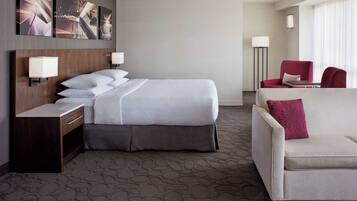 Quarto de hotel com uma cama grande, mesa de cabeceira com luminárias, um sofá e uma cadeira.