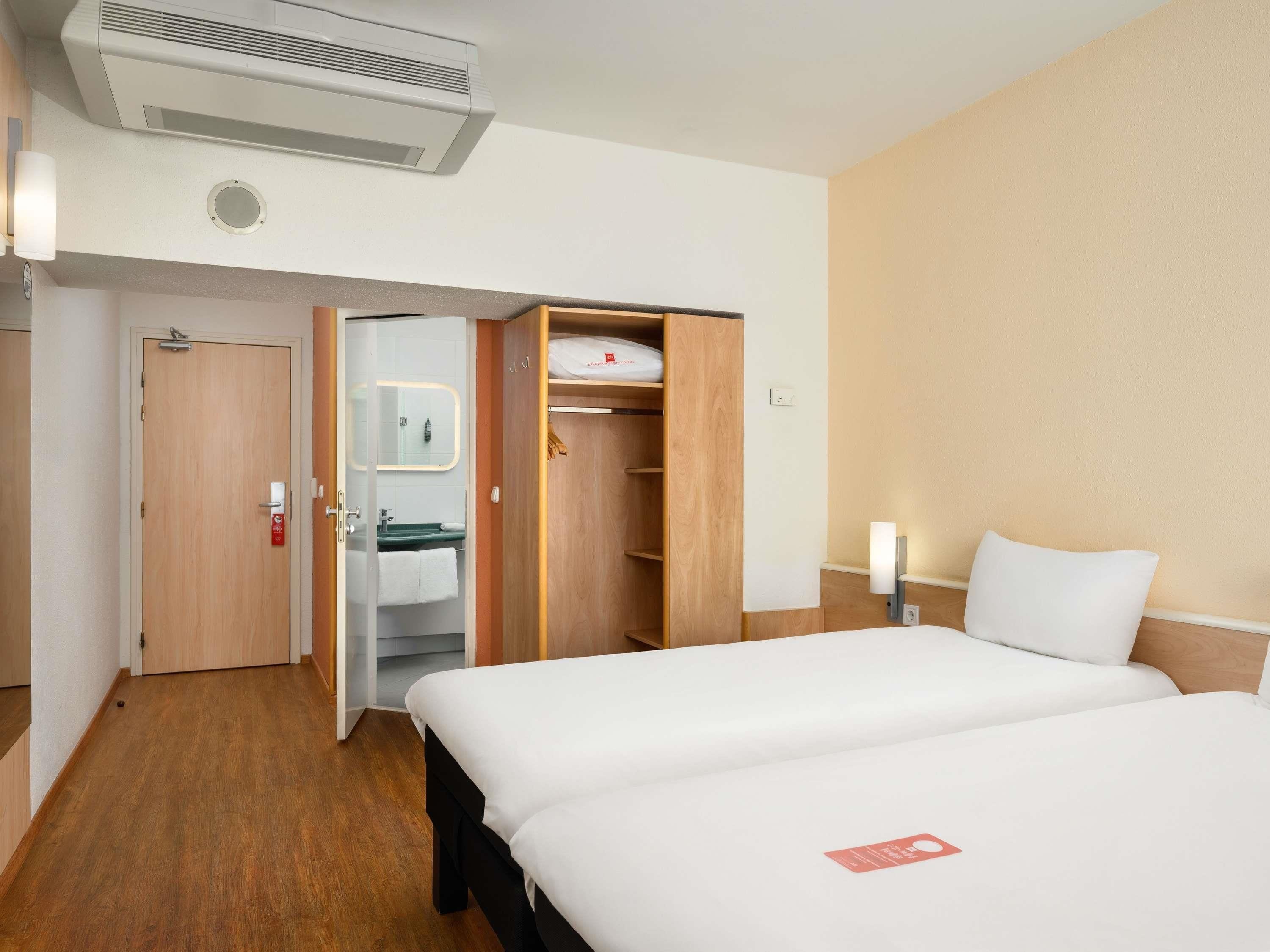 Quarto de hotel com cama, armário, espelho, pia e ar-condicionado no teto.