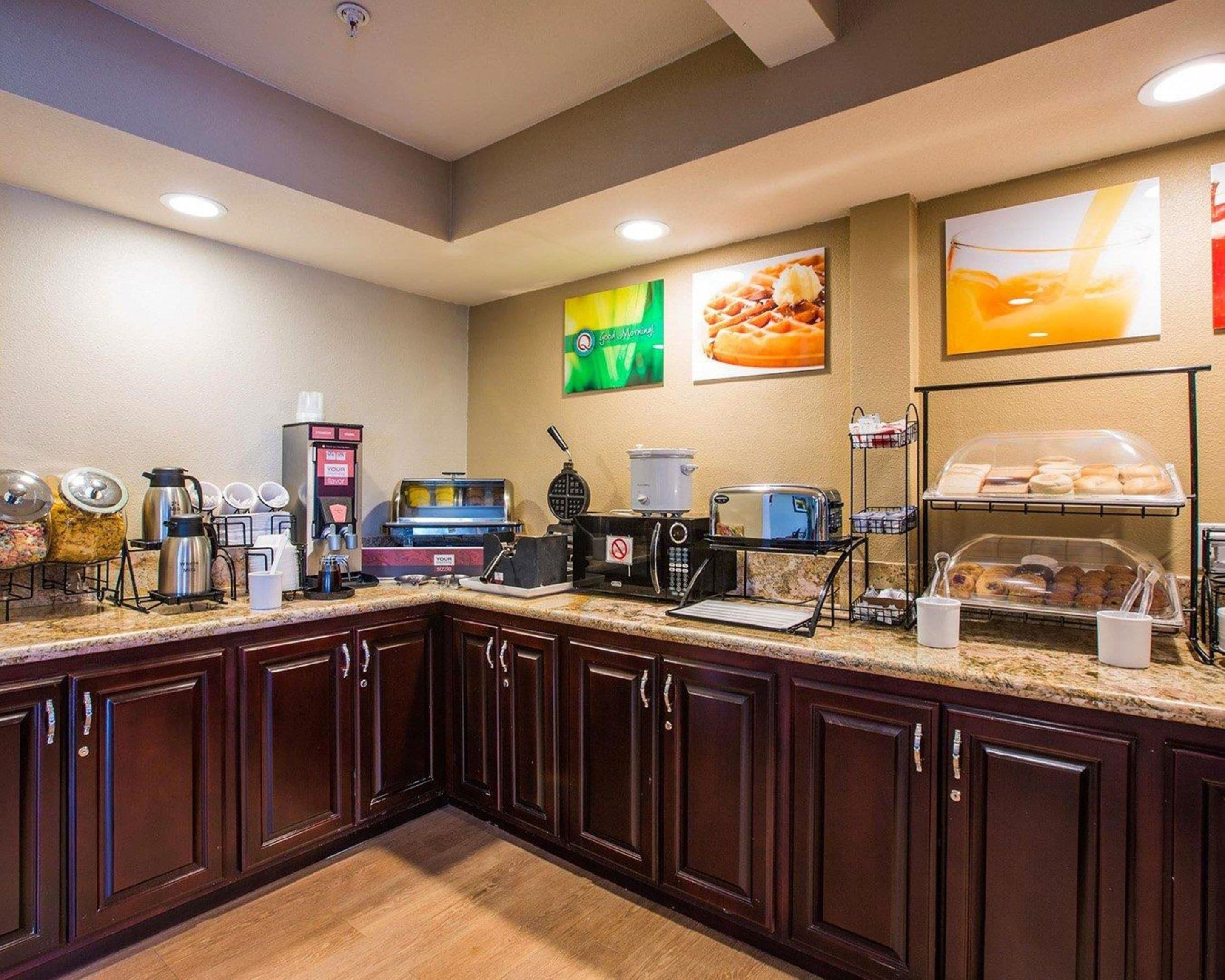 Espaço de café da manhã de hotel, com estação de café, torradeira e vitrine com doces.