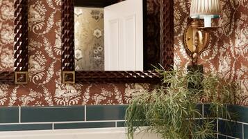 Casa de banho com lavatório branco, torneiras douradas e espelho com moldura estampada.