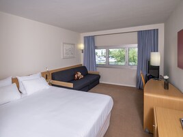 Quarto de hotel com uma cama grande, um sofá, uma escrivaninha e uma janela com cortinas.