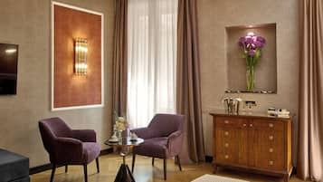 Quarto com sofá, duas poltronas, uma mesa redonda com um vaso de flores, um armário de madeira e uma televisão de tela plana na parede.