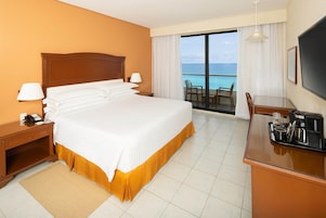 Quarto de hotel com uma cama grande, escrivaninha com cafeteira, televisão e varanda com vista para o mar.