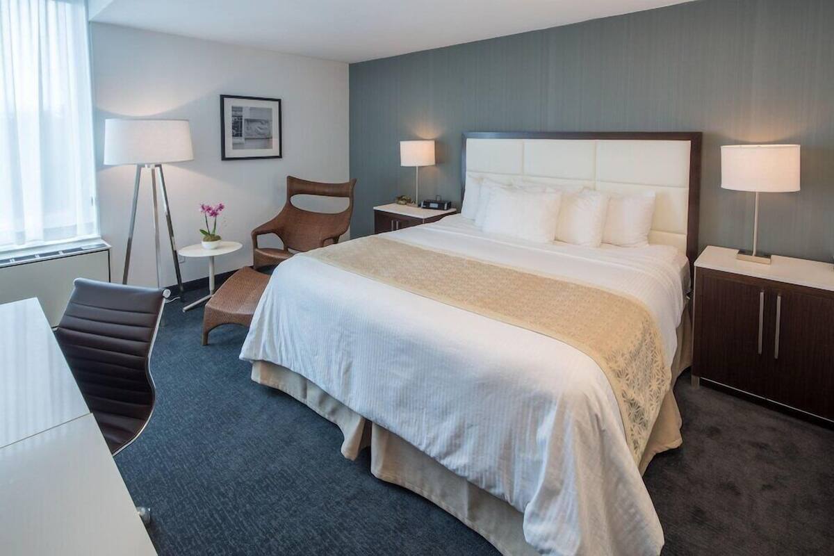 Quarto de hotel com uma cama grande, uma escrivaninha, uma cadeira, uma mesinha de centro e um abajur.