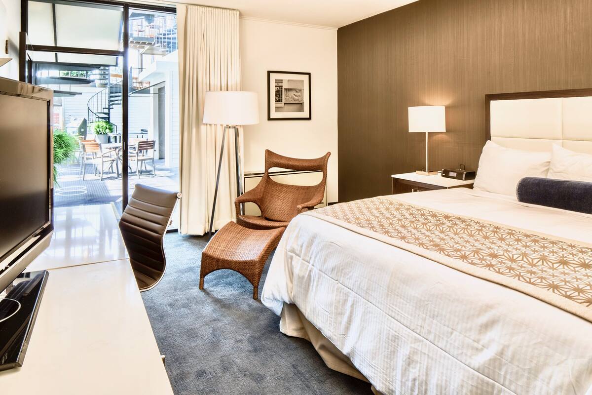 Quarto de hotel com cama, escrivaninha, cadeira, televisão e vista para o exterior.