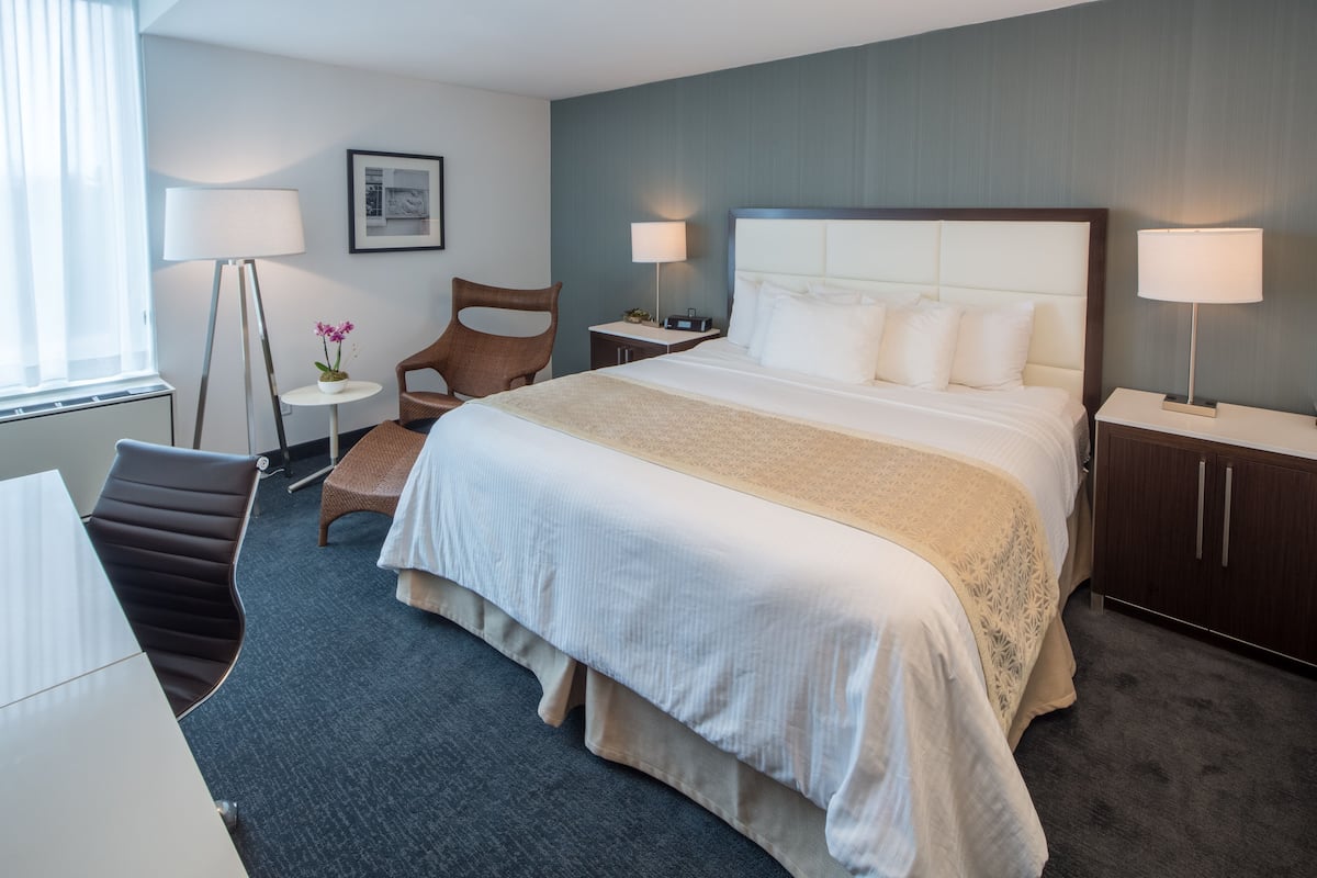 Quarto de hotel com uma cama grande, uma escrivaninha, uma cadeira, uma mesa pequena e um abajur.