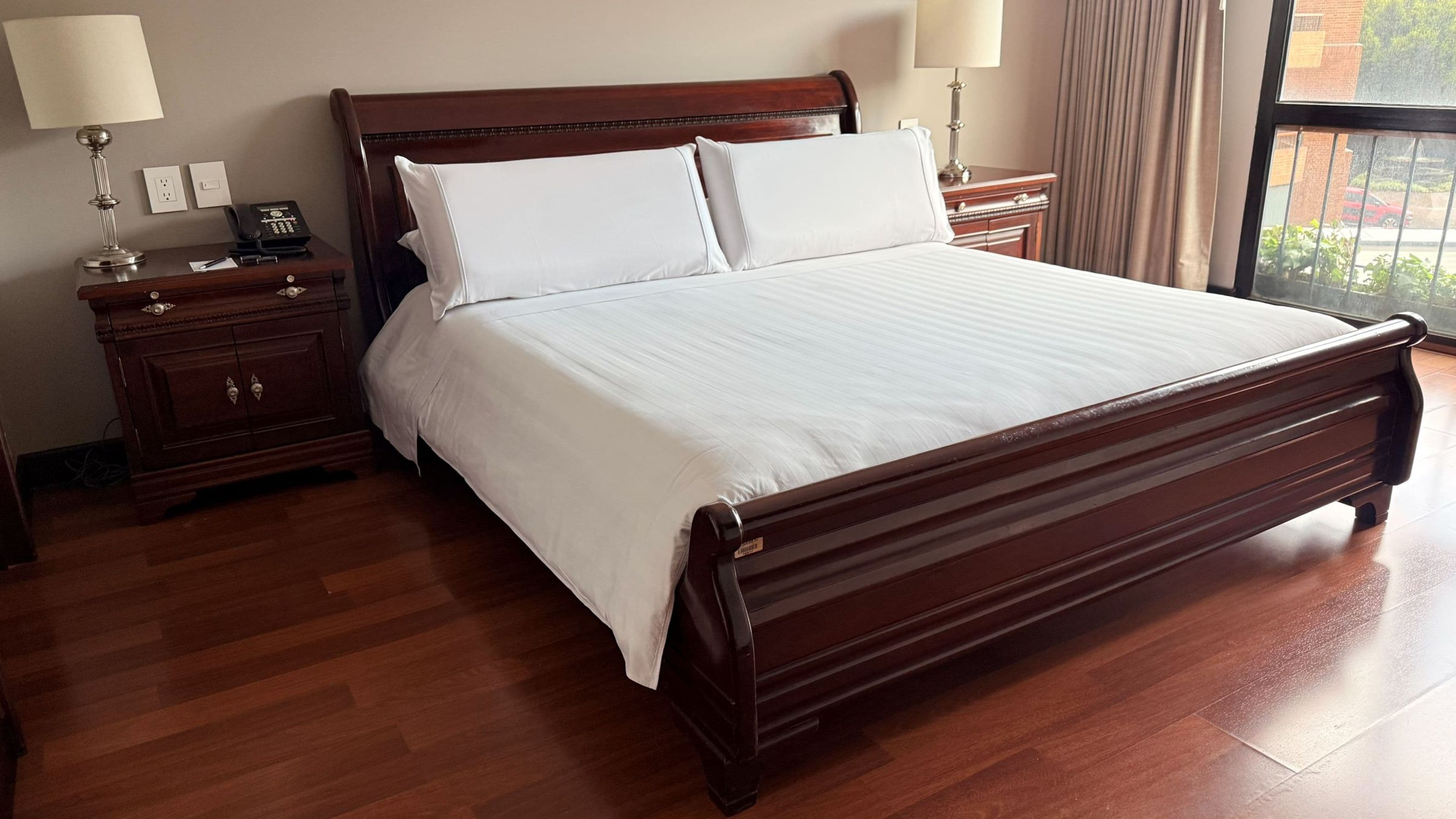 Quarto de hotel com cama de madeira, mesas de cabeceira e janela com vista exterior.