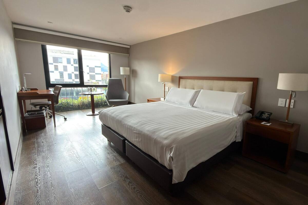 Quarto de hotel com uma cama grande, uma escrivaninha, uma cadeira e uma varanda com vista.