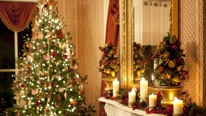 Uma árvore de Natal decorada, uma lareira com velas e um espelho em um quarto com iluminação acolhedora.