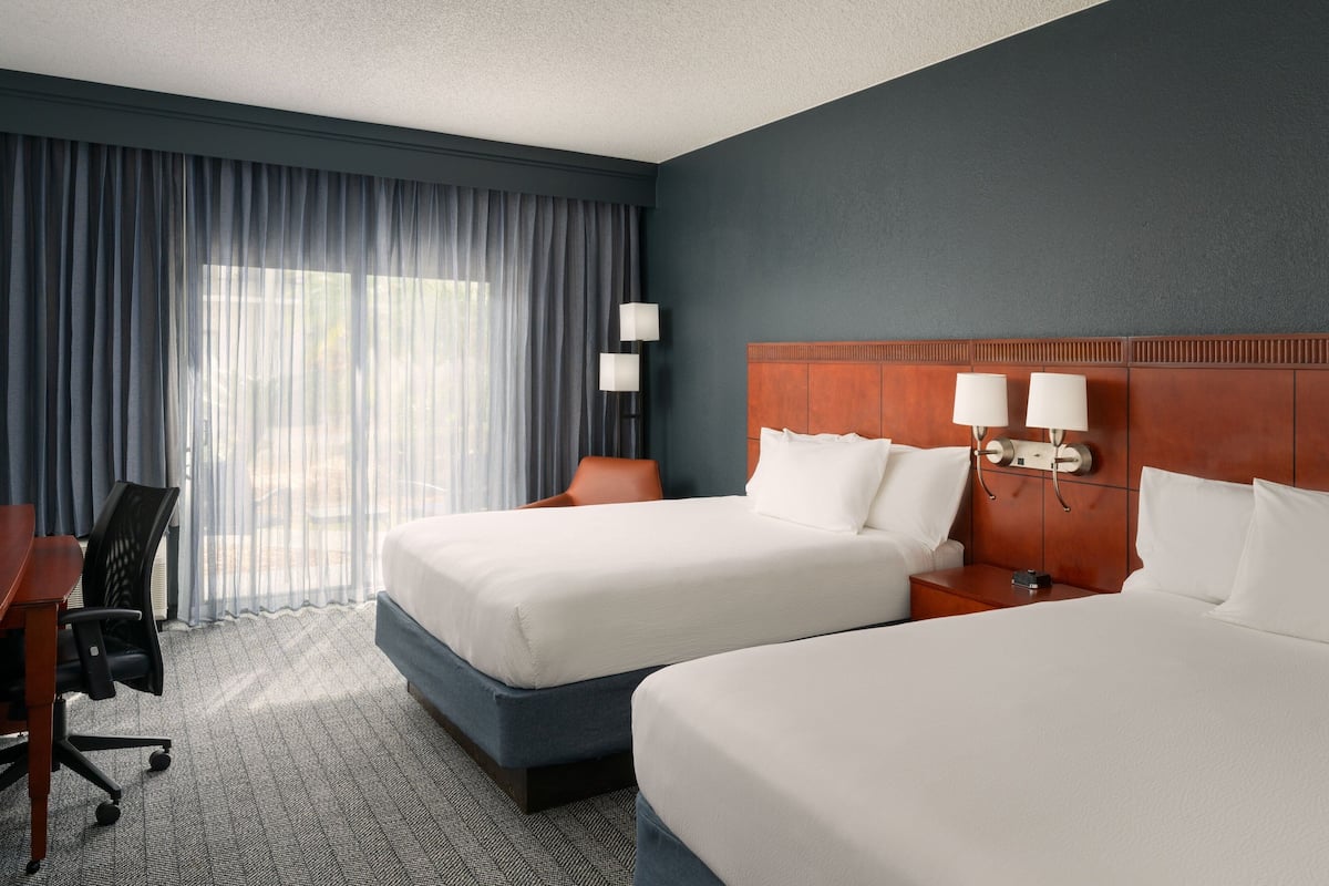 Quarto de hotel com duas camas, uma escrivaninha e uma cadeira.