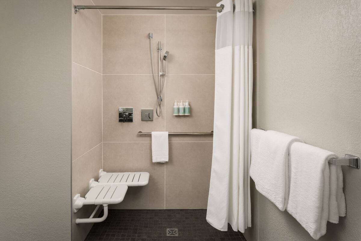 Casa de banho moderna com chuveiro, barra de apoio, porta-toalhas e um pequeno compartimento com produtos de higiene pessoal.