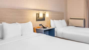 Quarto de hotel com duas camas, uma mesa de cabeceira com telefone e luminária fixa na parede.