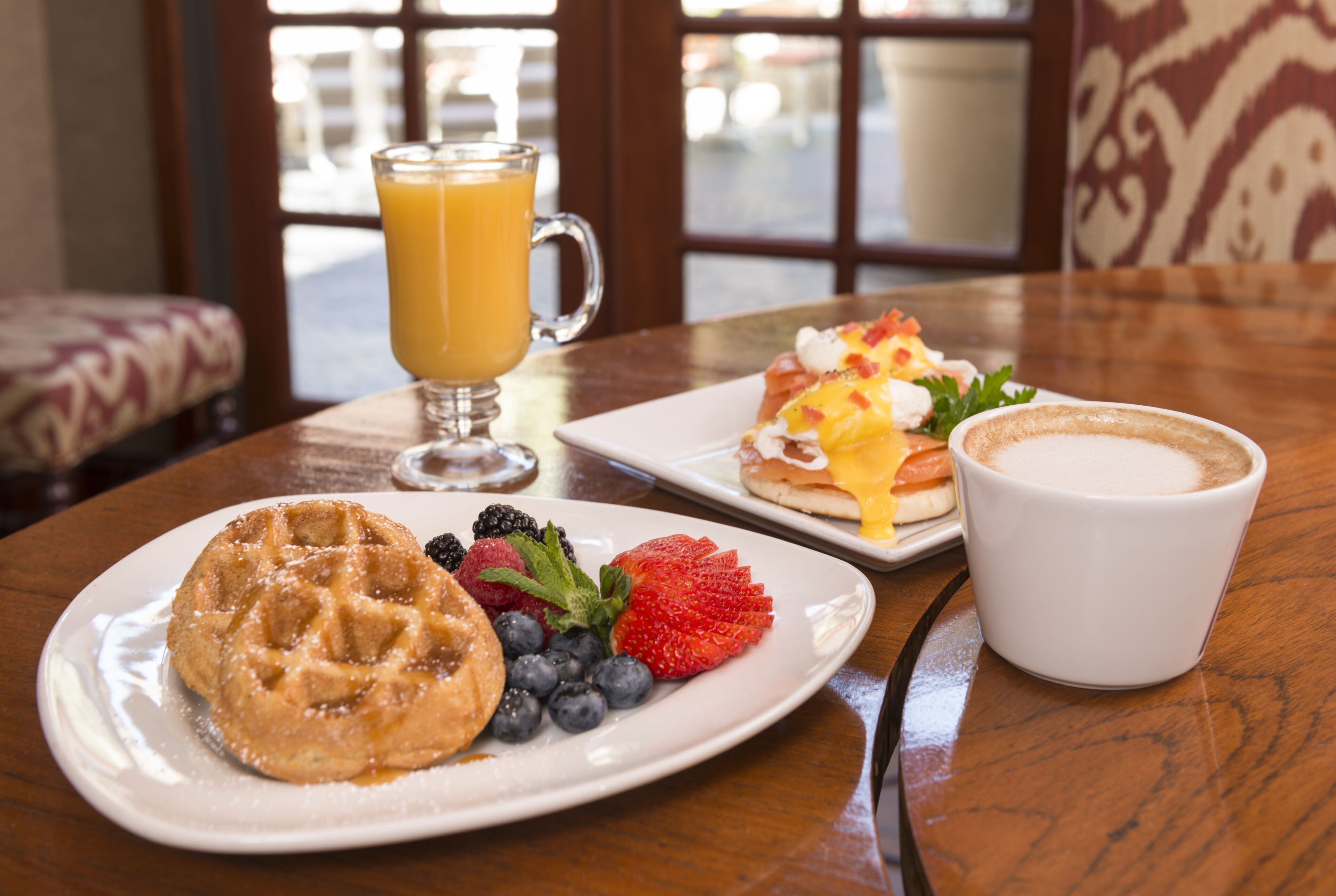 Mesa posta para o café da manhã, com waffle, frutas, ovos mexidos e café.