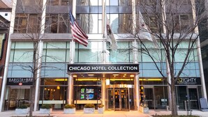 Edifício do Chicago Hotel Collection com fachada de vidro, bandeira americana e placas indicando Barista Bar e eventos Seighity.