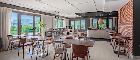 Uma área de refeições moderna, com mesas, cadeiras, cozinha e janelas amplas com vista para o exterior.