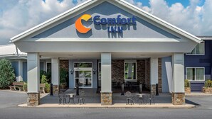 Um hotel Comfort Inn com design moderno, apresentando um logotipo marcante, entrada coberta com área de estar externa e fachada de pedra.