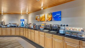 Espaço de café da manhã de hotel com armários de madeira, balcão de buffet e uma parede com a inscrição 'RISE & SHINE'.