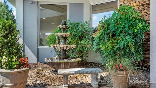 Um banco de pedra, uma fonte em terraços e plantas em vasos num pátio.